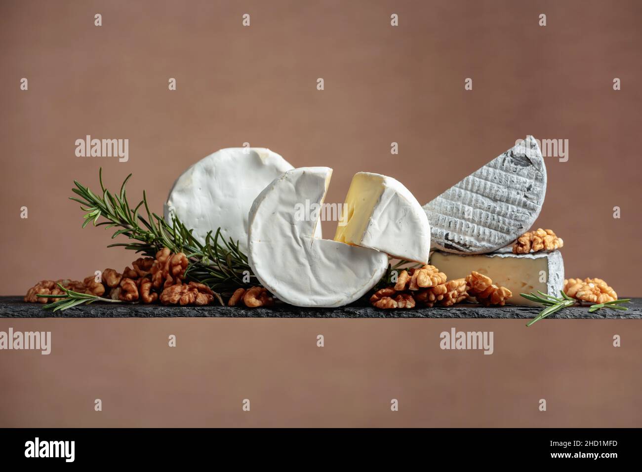 Soft cheeses with walnuts and rosemary on a brown background. Copy ...