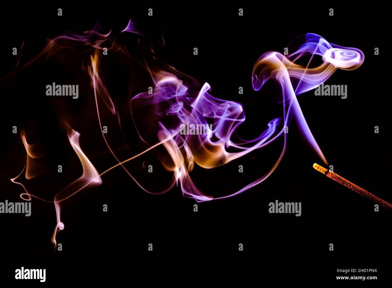 An aroma stick burns and smokes. Colored smoke is filmed in slow motion ...