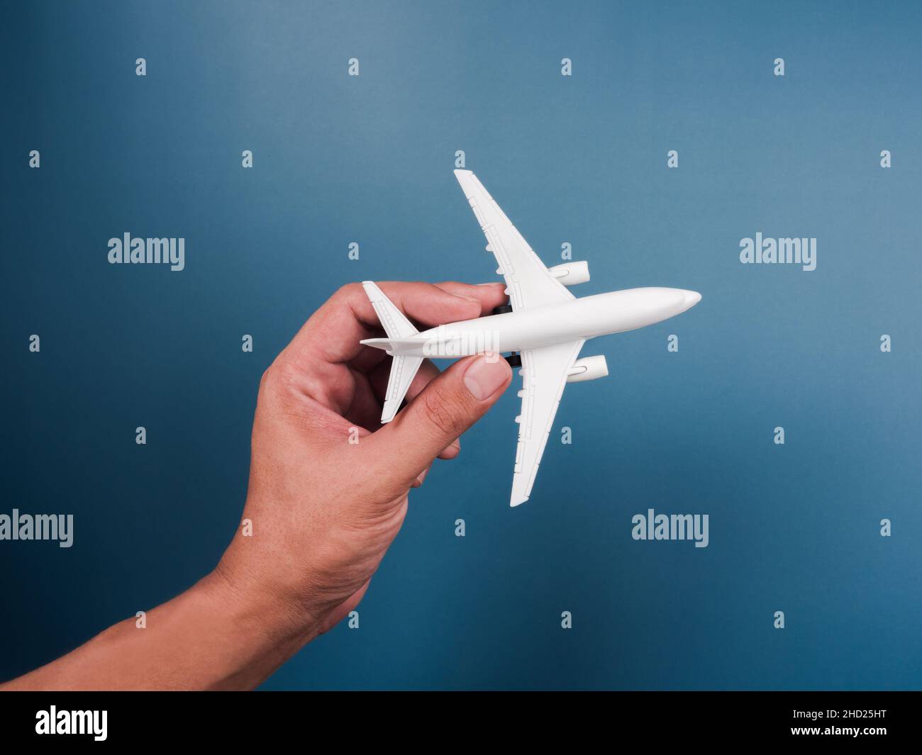 Hand holding white plane toy model on a blue background, top view ...