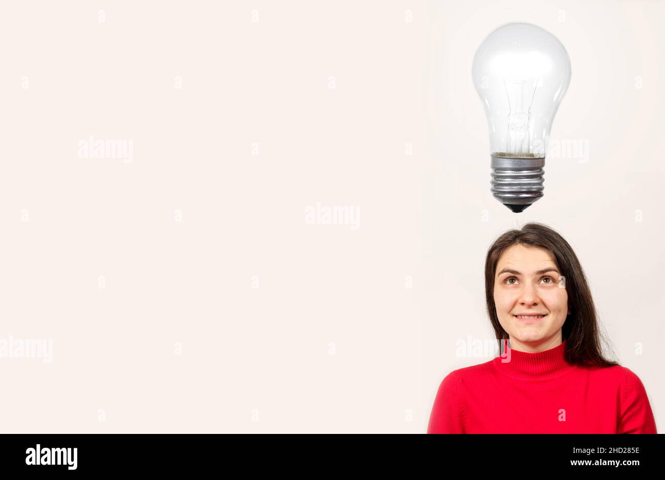 A woman looks at a glowing light bulb above her head, an idea and an ...
