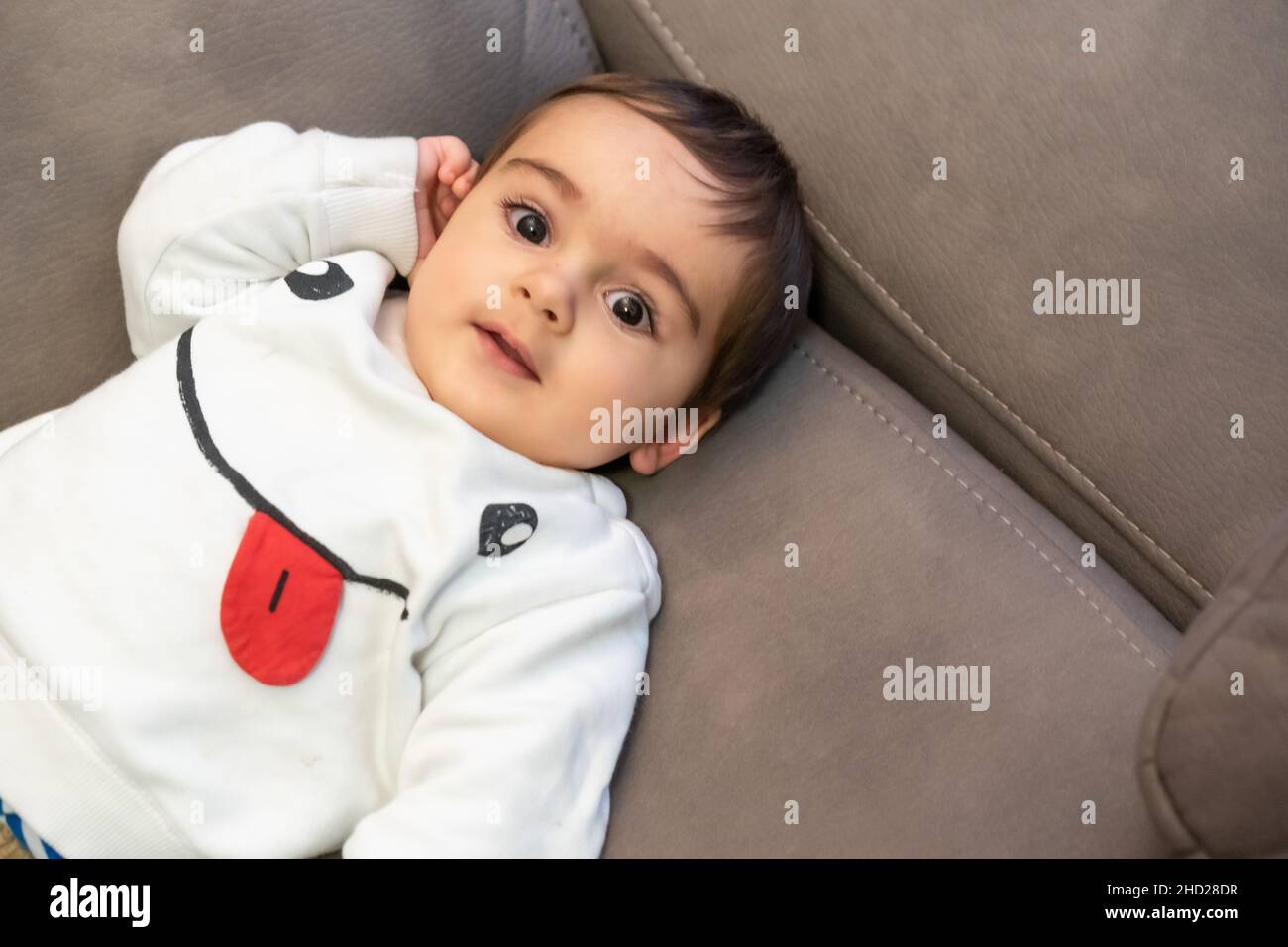 Baby crying with the pain of his first teeth, lying on the sofa at home ...