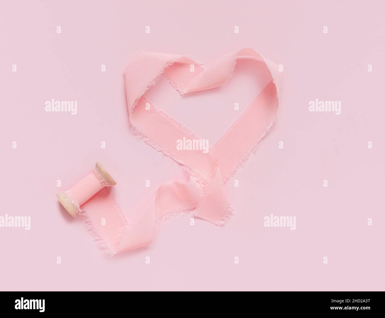 Pink silk ribbon heart with bobbin light pink background flat lay ...