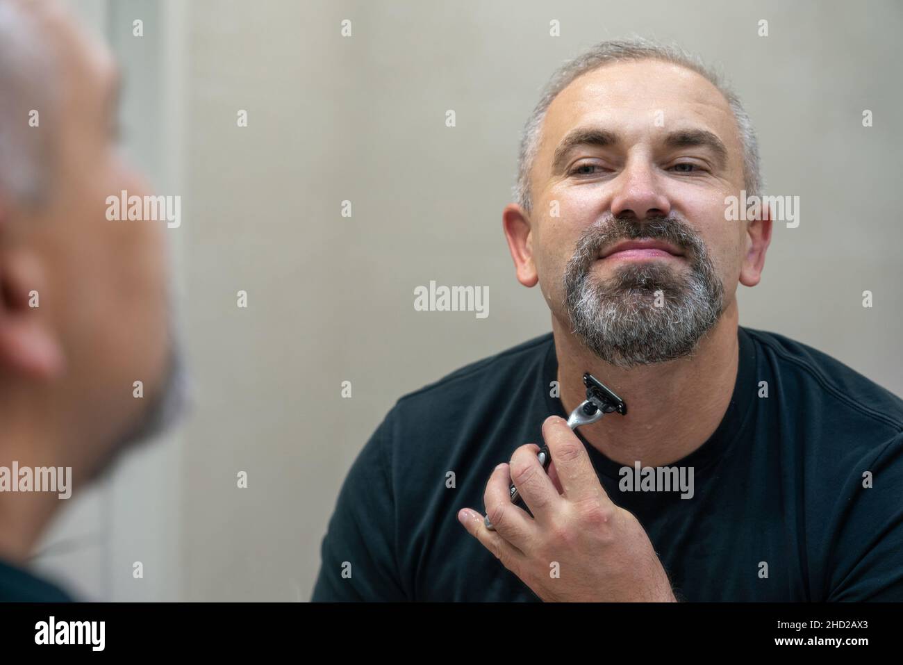 Charming middle aged man shaving his beard and moustache off in front ...