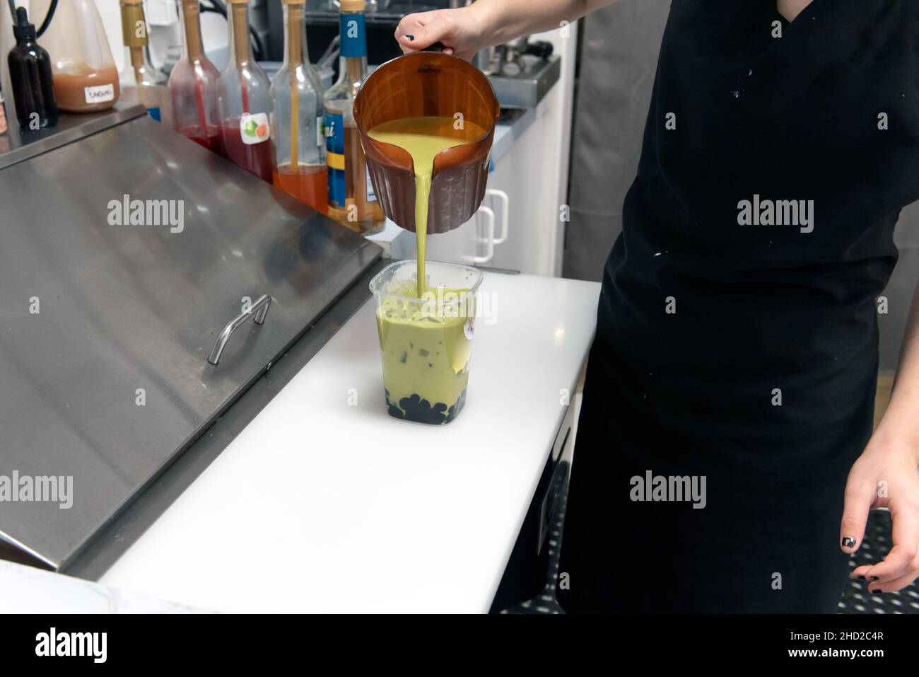 Hands pouring smoothie boba ingredients from a pitcher into the cup for ...
