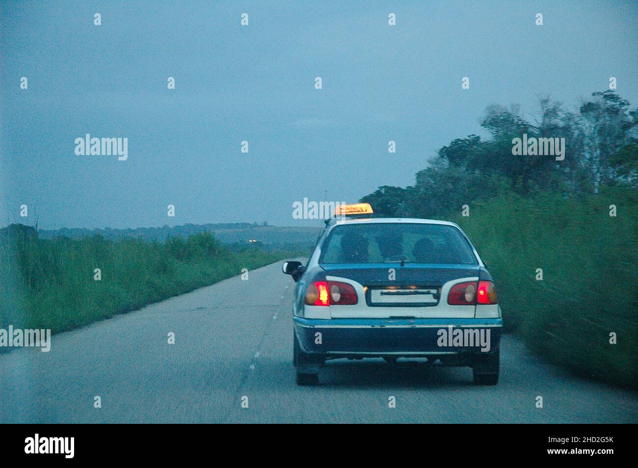Rear view of a taxi on the street in Congo at dusk with palm trees. Way ...