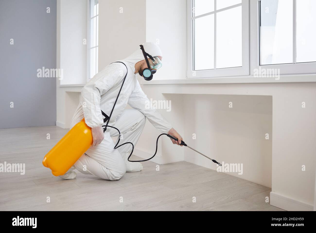 Pest control exterminator in protective mask and suit spraying ...