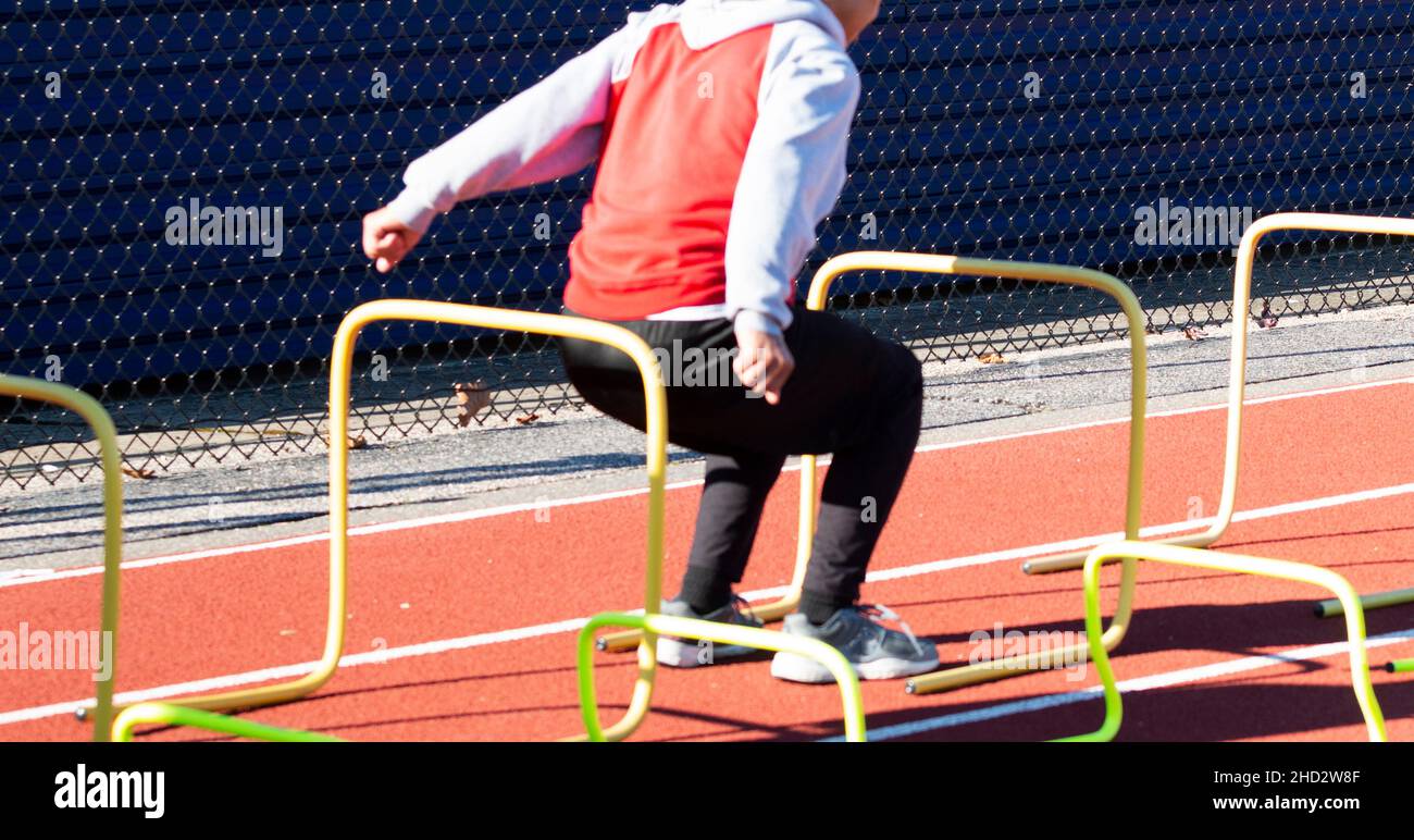 High school bly landing as he is jumping over yellow hurdles during ...