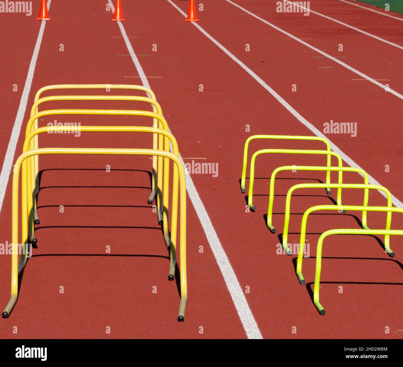 A red track set up for speed and agility work with different sized plastic yellow hurdles in ...