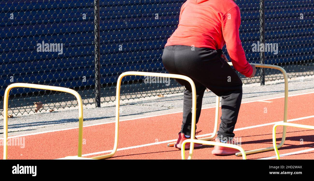 High school boy jumping over yellow plastic hurdles during track ...