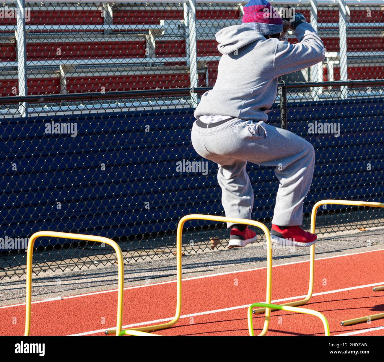 A high school boy track and field athlete jumping over yellow hurdles ...