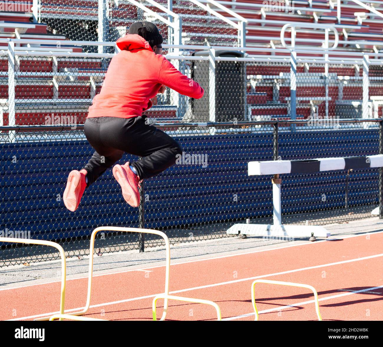 A high school boy is jumping high over yellow hurdles on a red track in ...