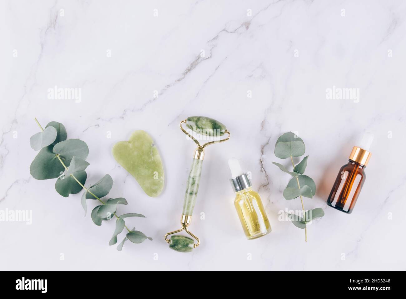 Flat lay composition with jade gua sha facial roller with beauty serum ...
