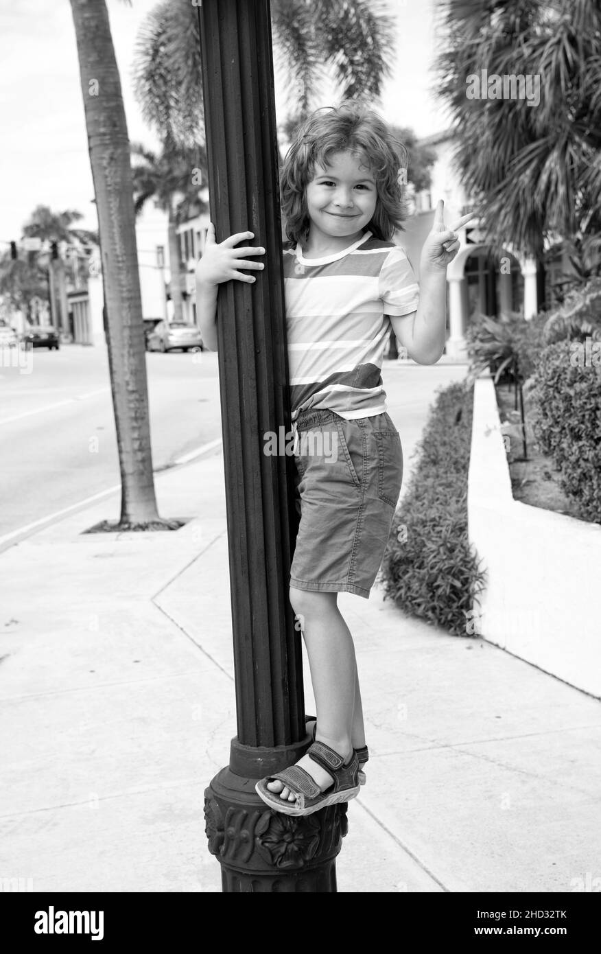 Boys plays. Happy boy stand on lamppost. Boy child smile showing V sign ...