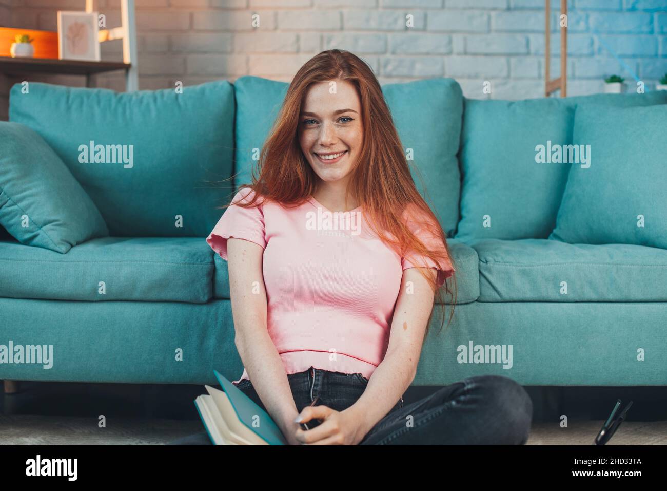 Front view of a woman sitting on floor leaning on sofa at home ...