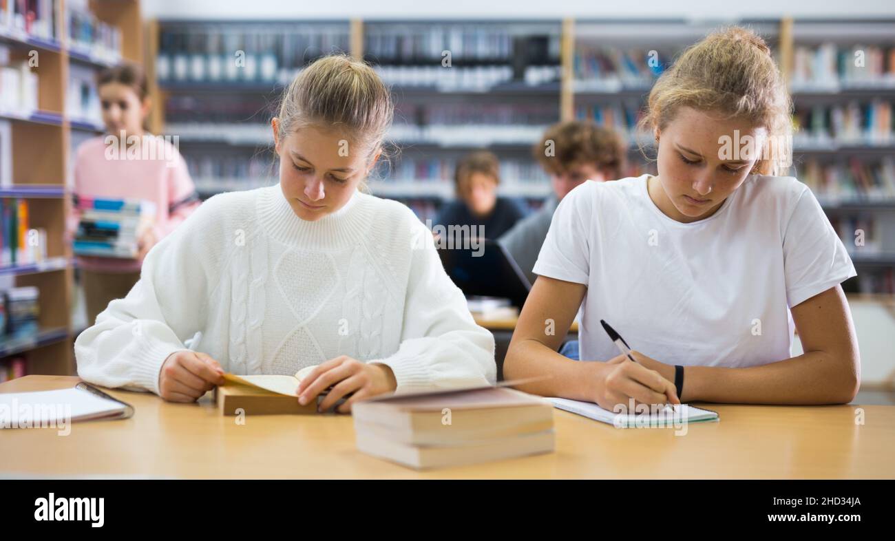Two schoolgirls take notes in a exercise book of the necessary material ...