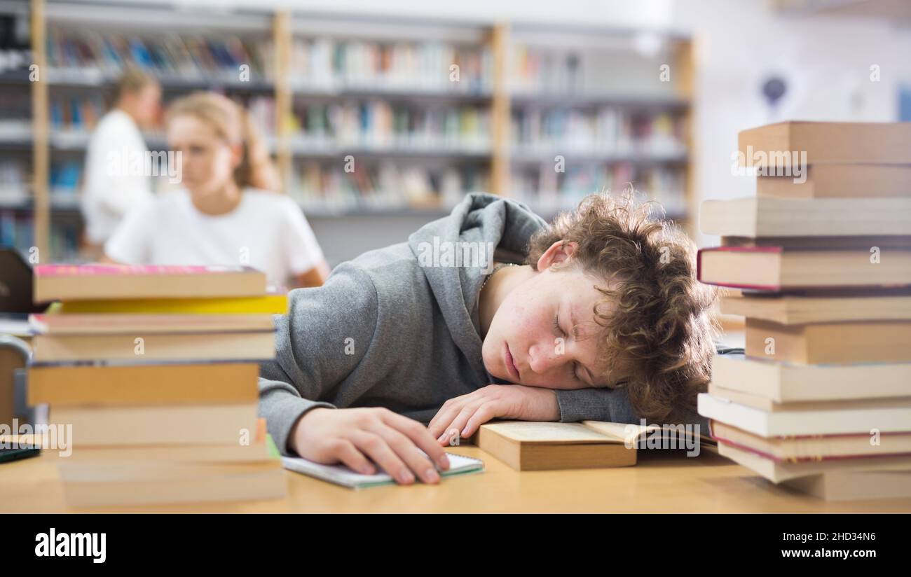 Tired teenager boy in library Stock Photo - Alamy