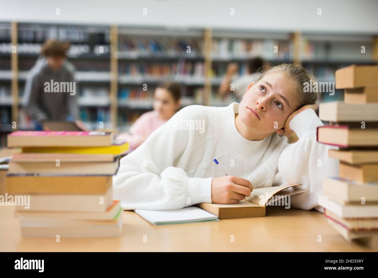 Bored teenage girl trying to prepare for exam in library Stock Photo ...