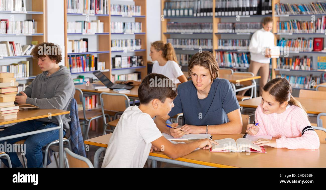 Group of schoolchildren reading books together in library and preparing ...