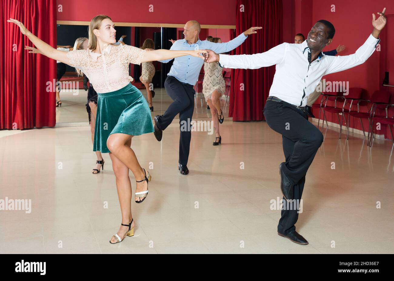 Young positive people dancing twist in pairs at dance hall together ...