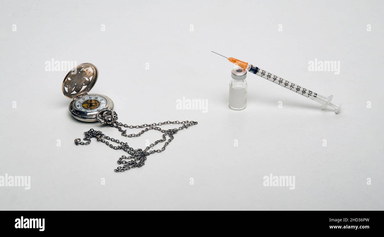 Antique clock, next to a vial and a syringe, indicating that it is time ...