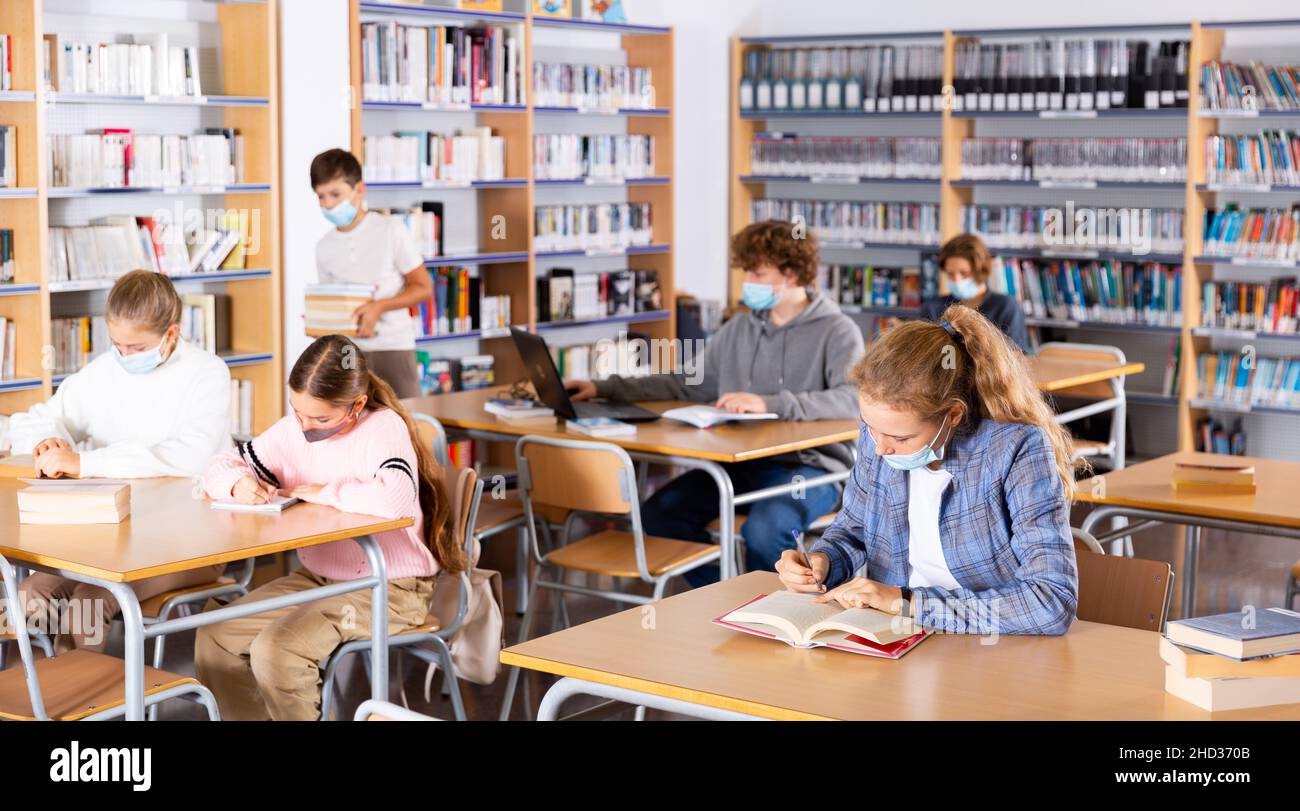 Fifteen-year-old girl in a mask writes out a synopsis from a textbook ...