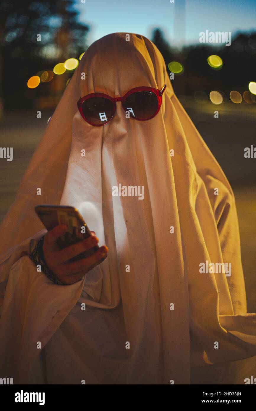 Vertical shot of a person in a fun ghost costume and sunglasses using ...