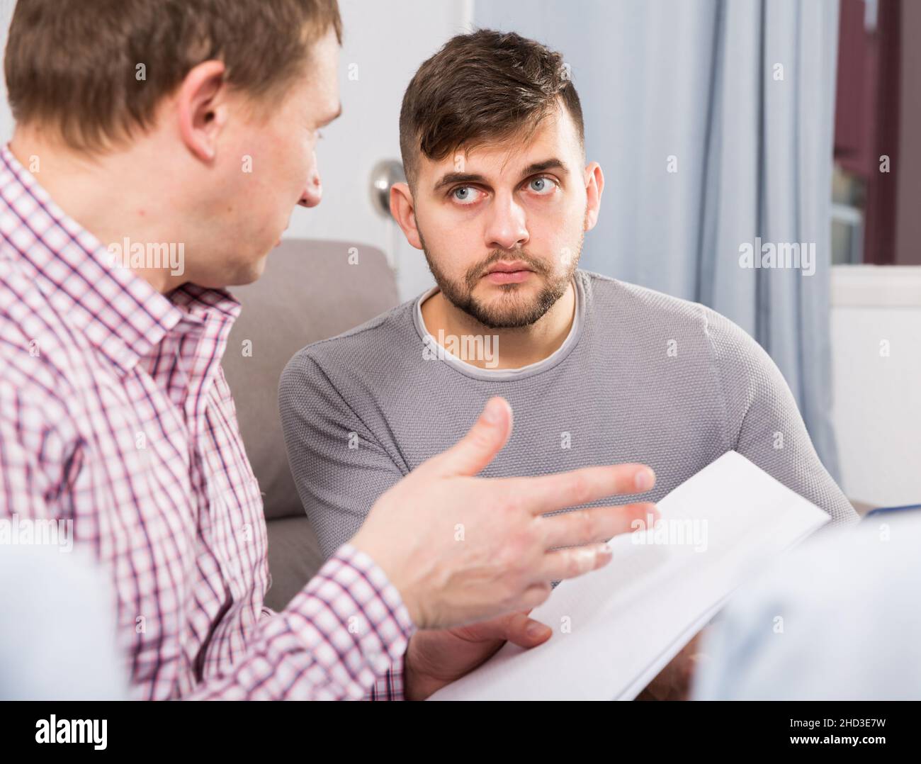 Man worriedly discussing documents with friend on sofa at home Stock ...