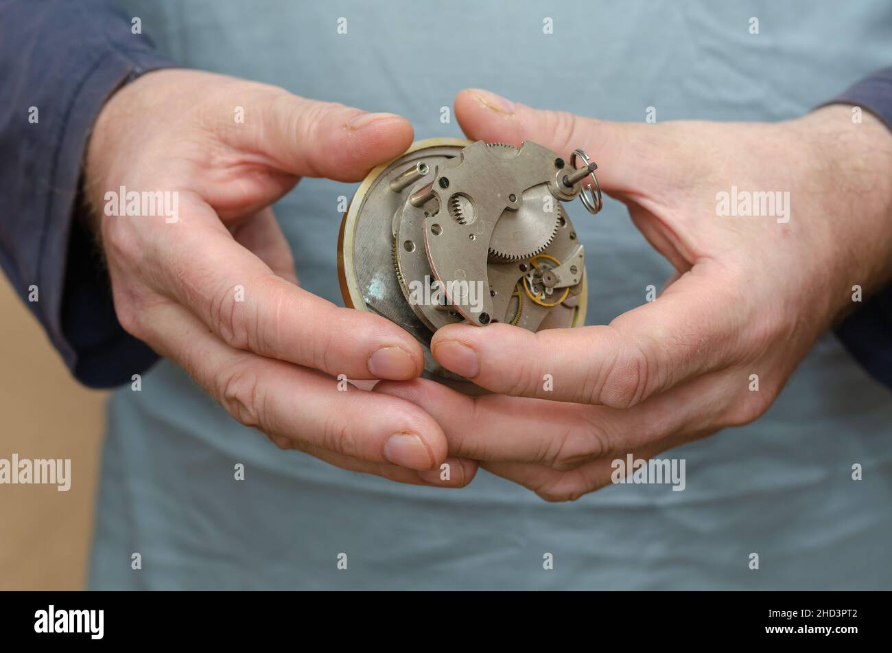 Two hands hold the mechanism of a table clock. A man is holding the ...