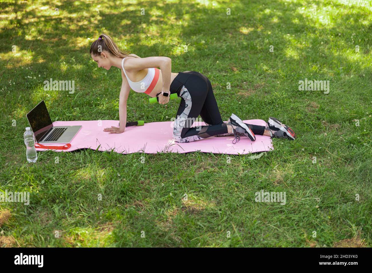 Smiling lady does exercise with dumbbell watching video traing in park ...