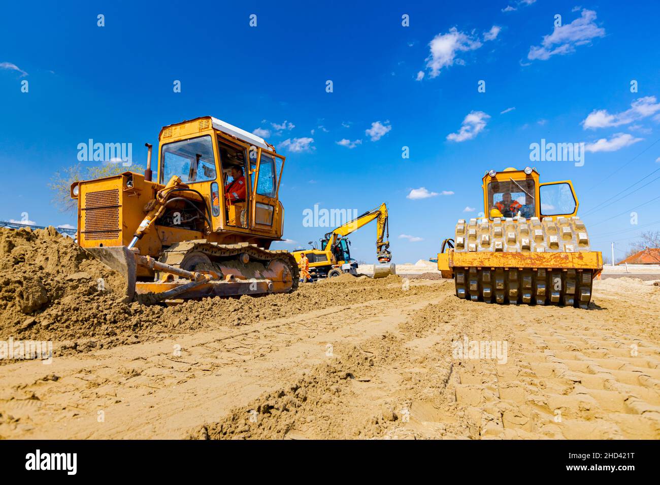 Road roller with spikes and bulldozer are compacting, leveling sand for ...