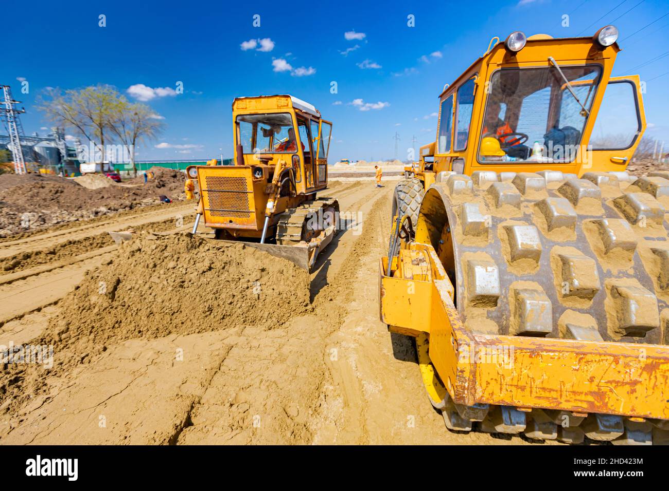Road roller with spikes and bulldozer are compacting, leveling sand for ...
