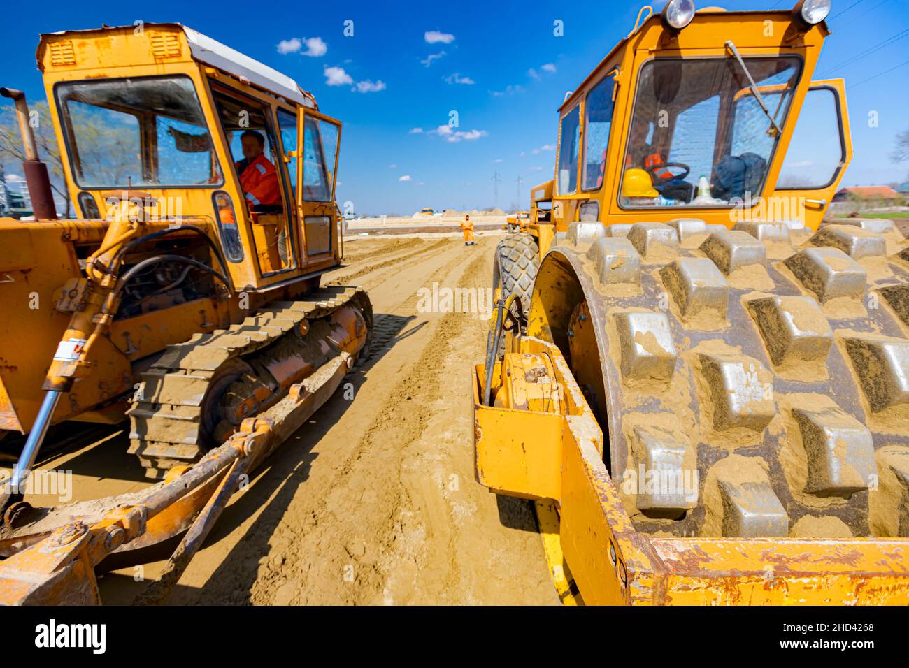 Road roller with spikes and bulldozer are compacting, leveling sand for ...