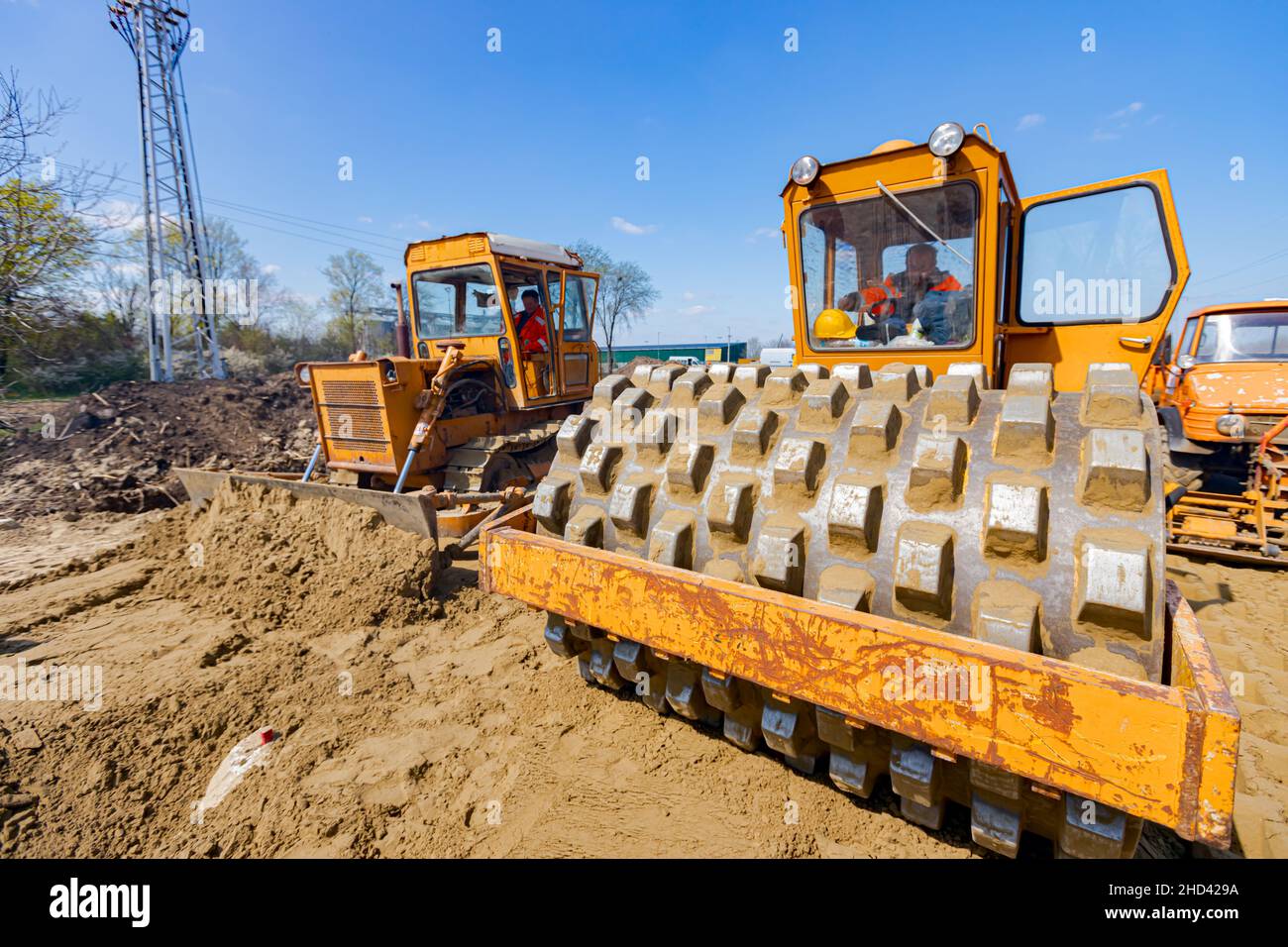 Road roller with spikes and bulldozer are compacting, leveling sand for ...