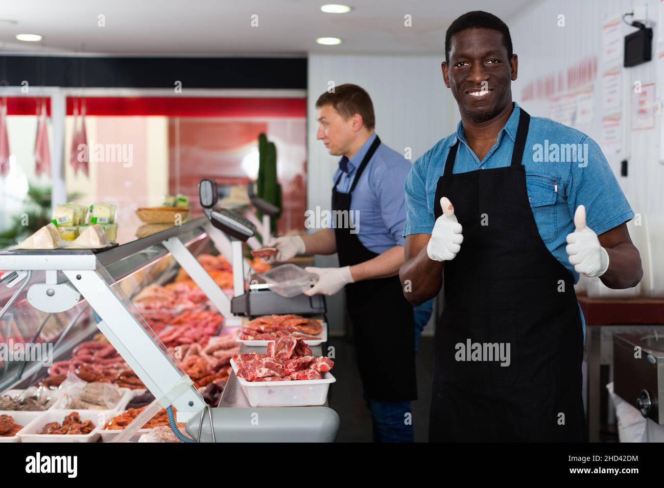 Happy African American seller of butcher store standing behind counter ...