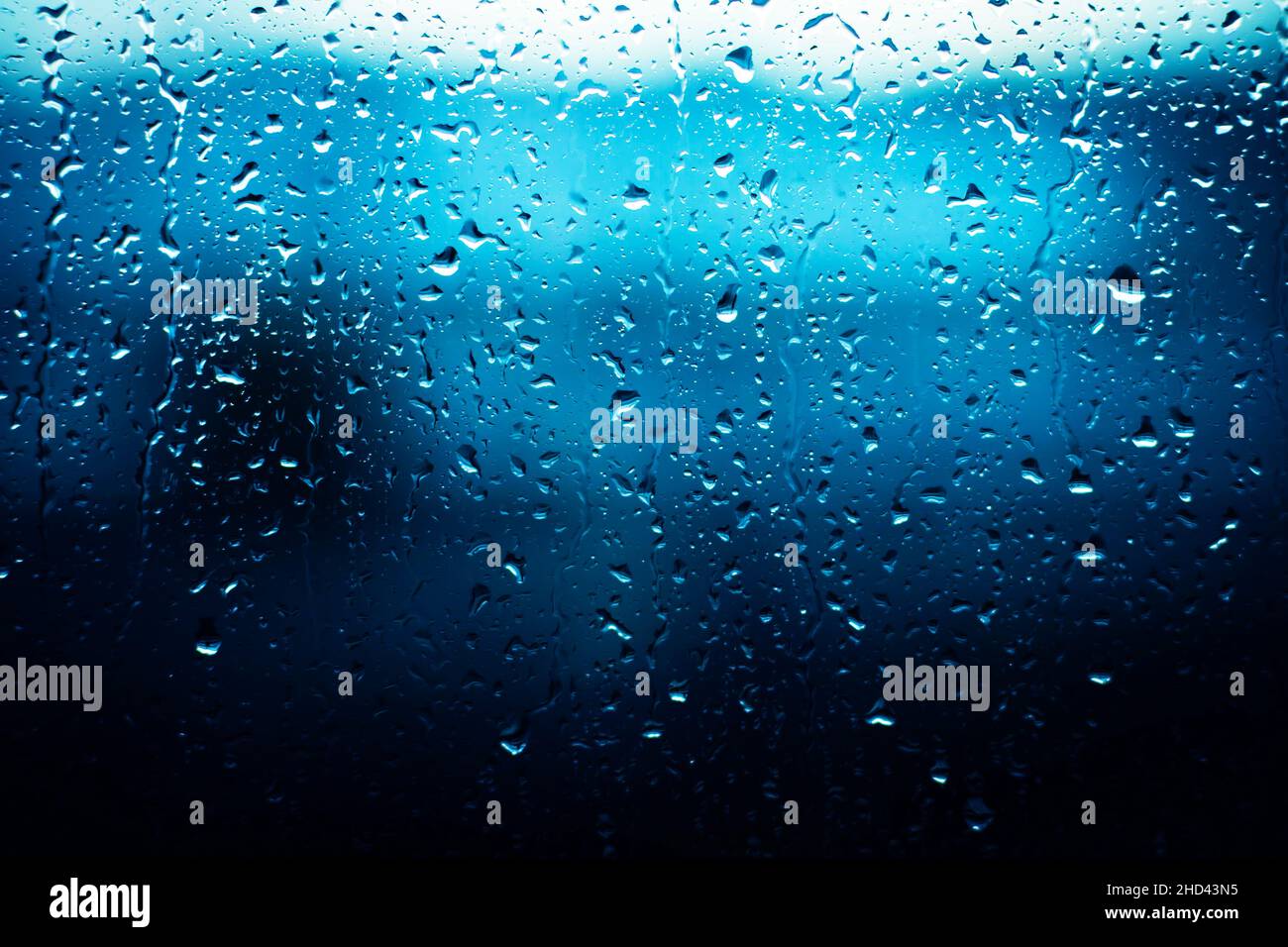 The transparent glass of the window is covered with dripping drops of ...