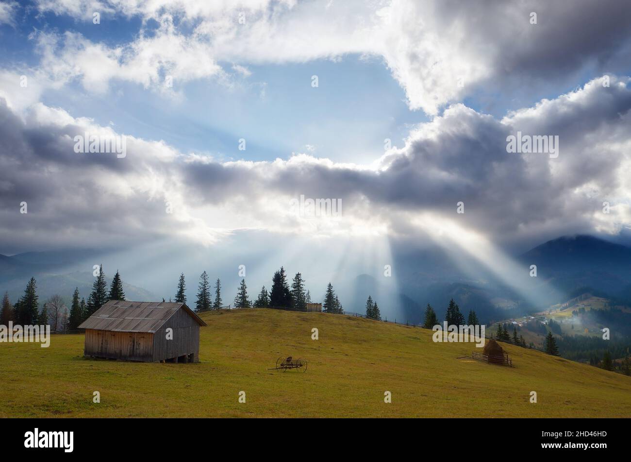Rural landscape with beautiful sun rays through the clouds. Wooden hut ...