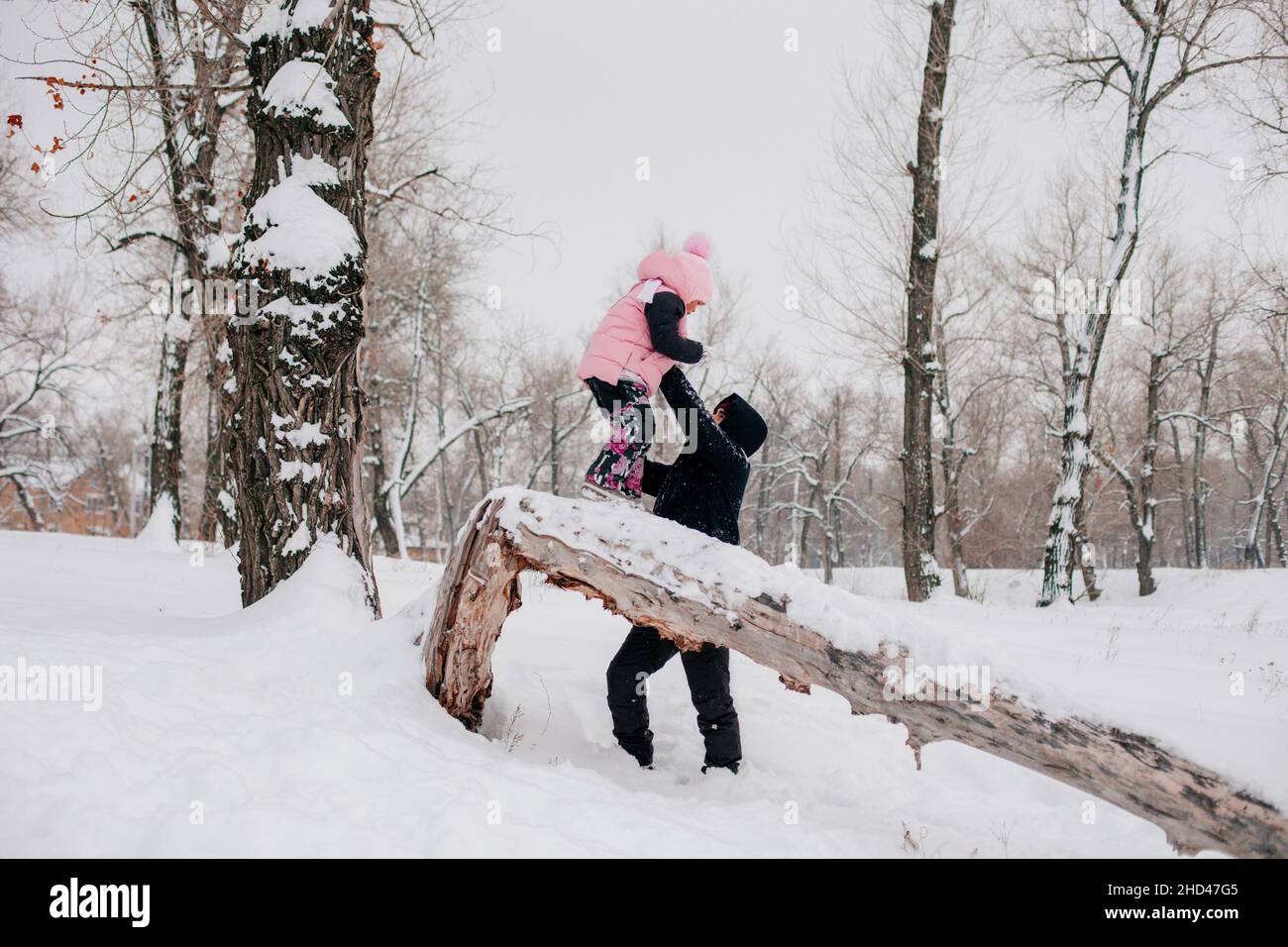 female kid standing on tree log about to jump off wearing pink winter ...