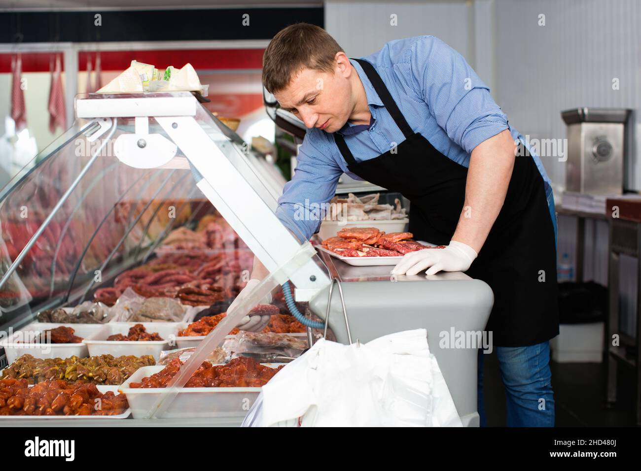 Smiling butcher standing in butcher shop with tray of fresh raw meat ...