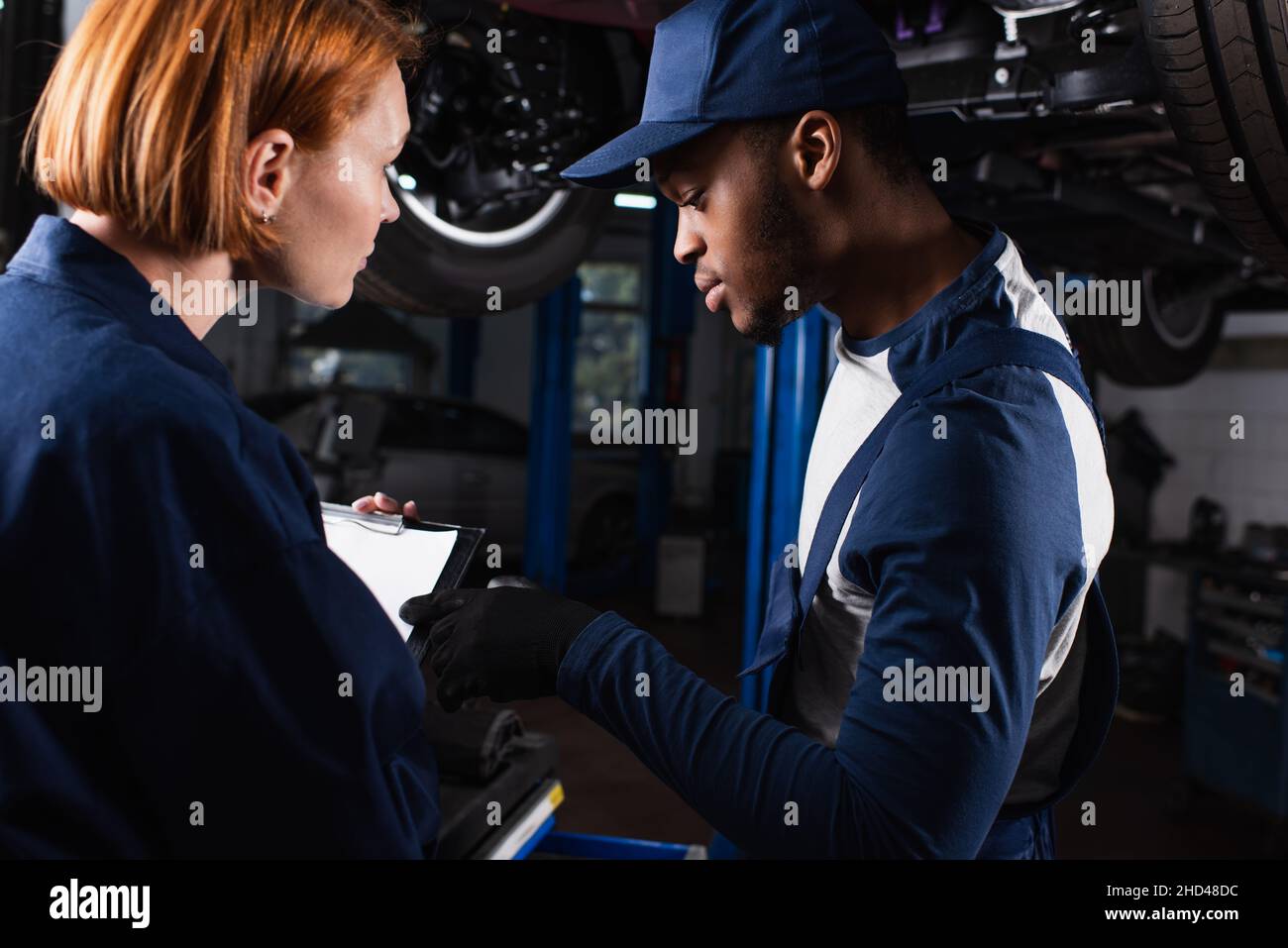 African american mechanic pointing at clipboard near colleague in car ...