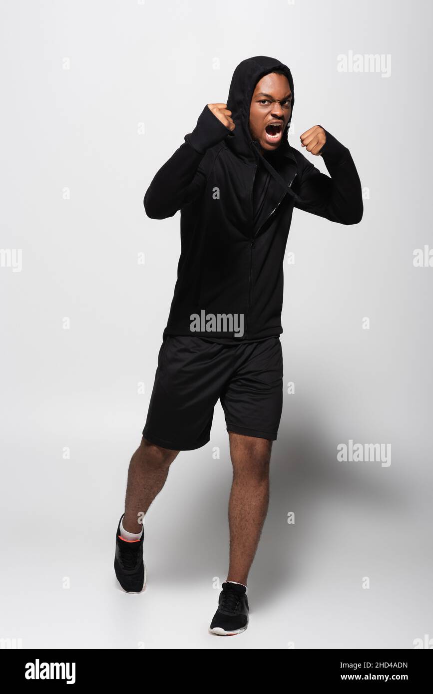 full length of angry african american man in hoodie fighting on grey ...