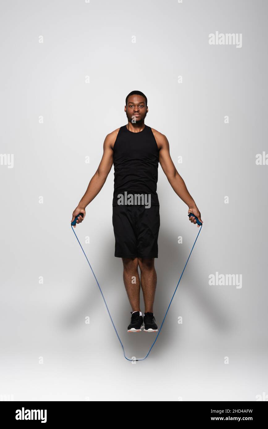 full length of african american sportsman jumping with skipping rope on grey Stock Photo - Alamy