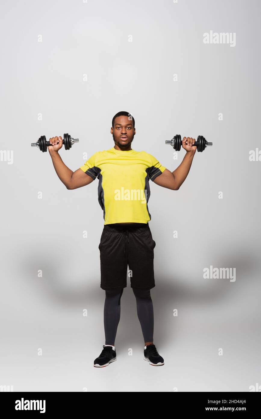 full length of african american sportsman working out with heavy dumbbells on grey Stock Photo ...