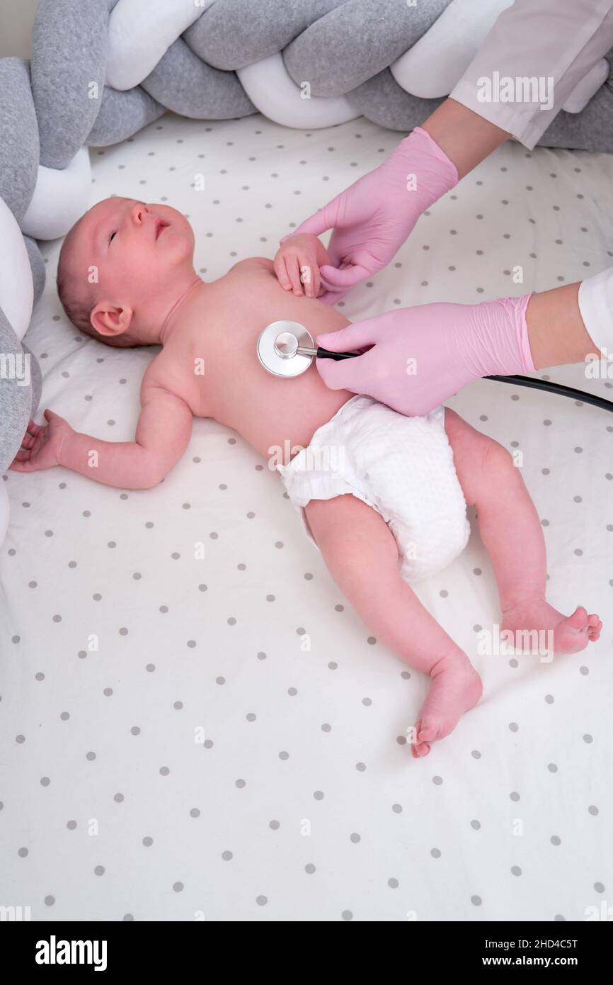 Woman doctor listens with a stethoscope to a newborn baby. Nurse checks ...