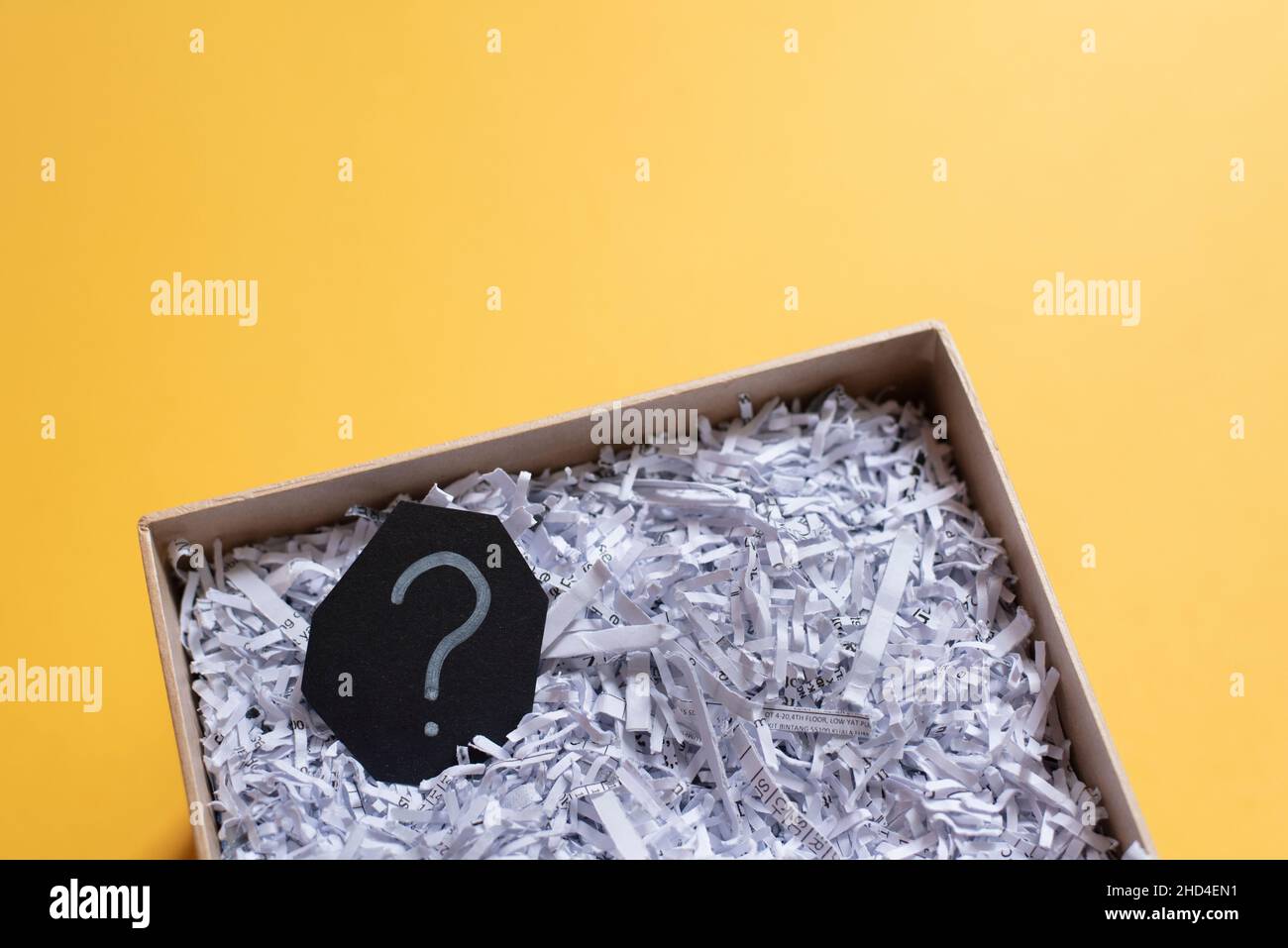 Question mark and shredded paper in abox against yellow background ...