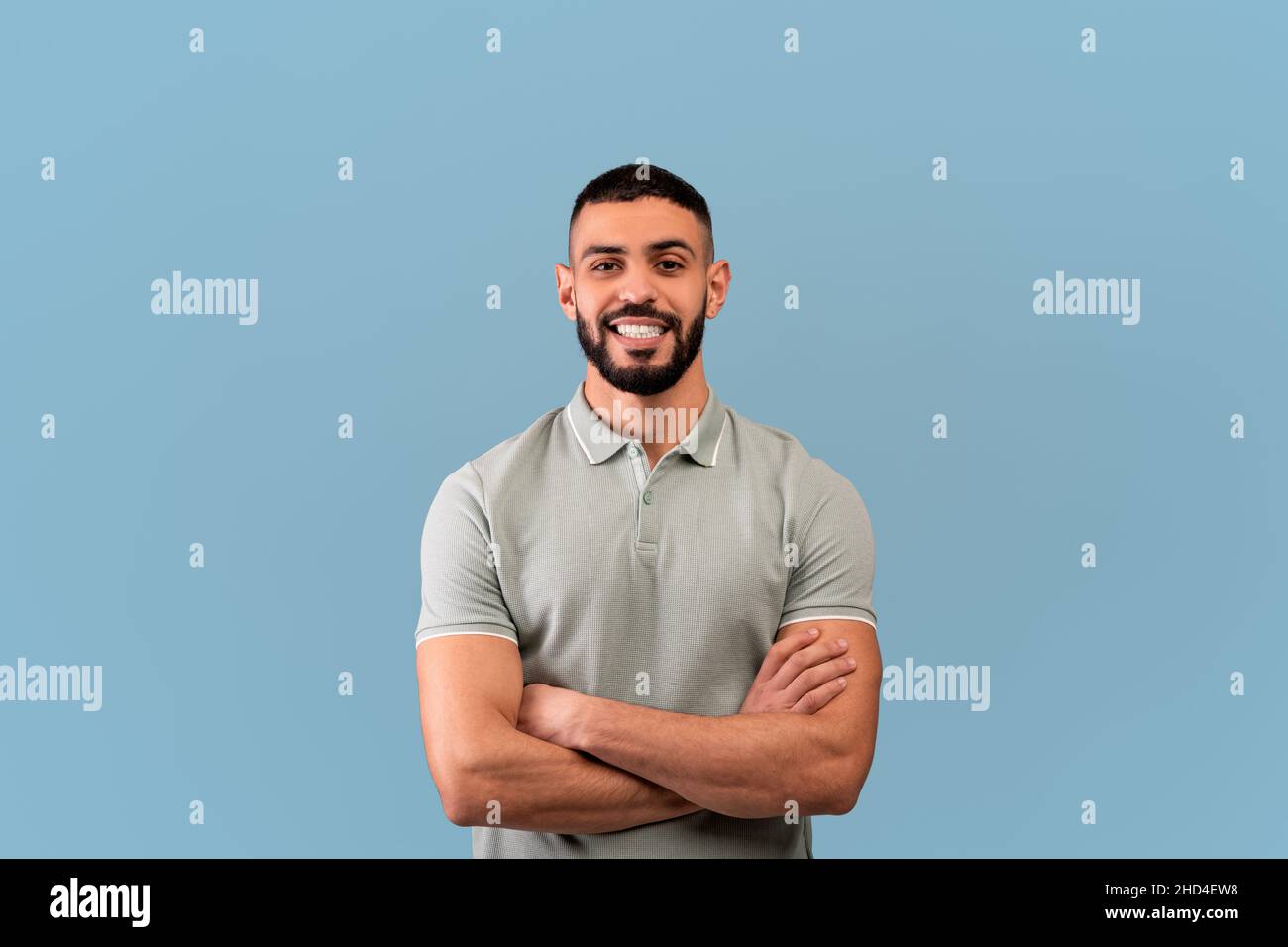 Happy arab guy smiling to camera, crossing hands and posing over blue ...