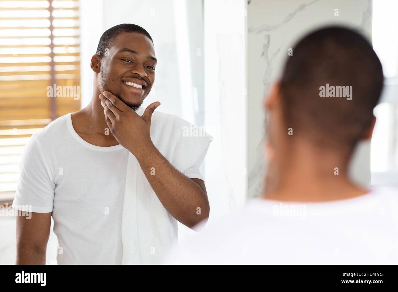 Male Skincare. Handsome Black Guy Looking In Mirror In Bathroom ...