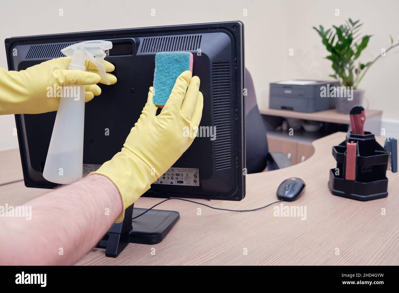 Cleaning the office, a janitor in yellow gloves wipes monitor and ...