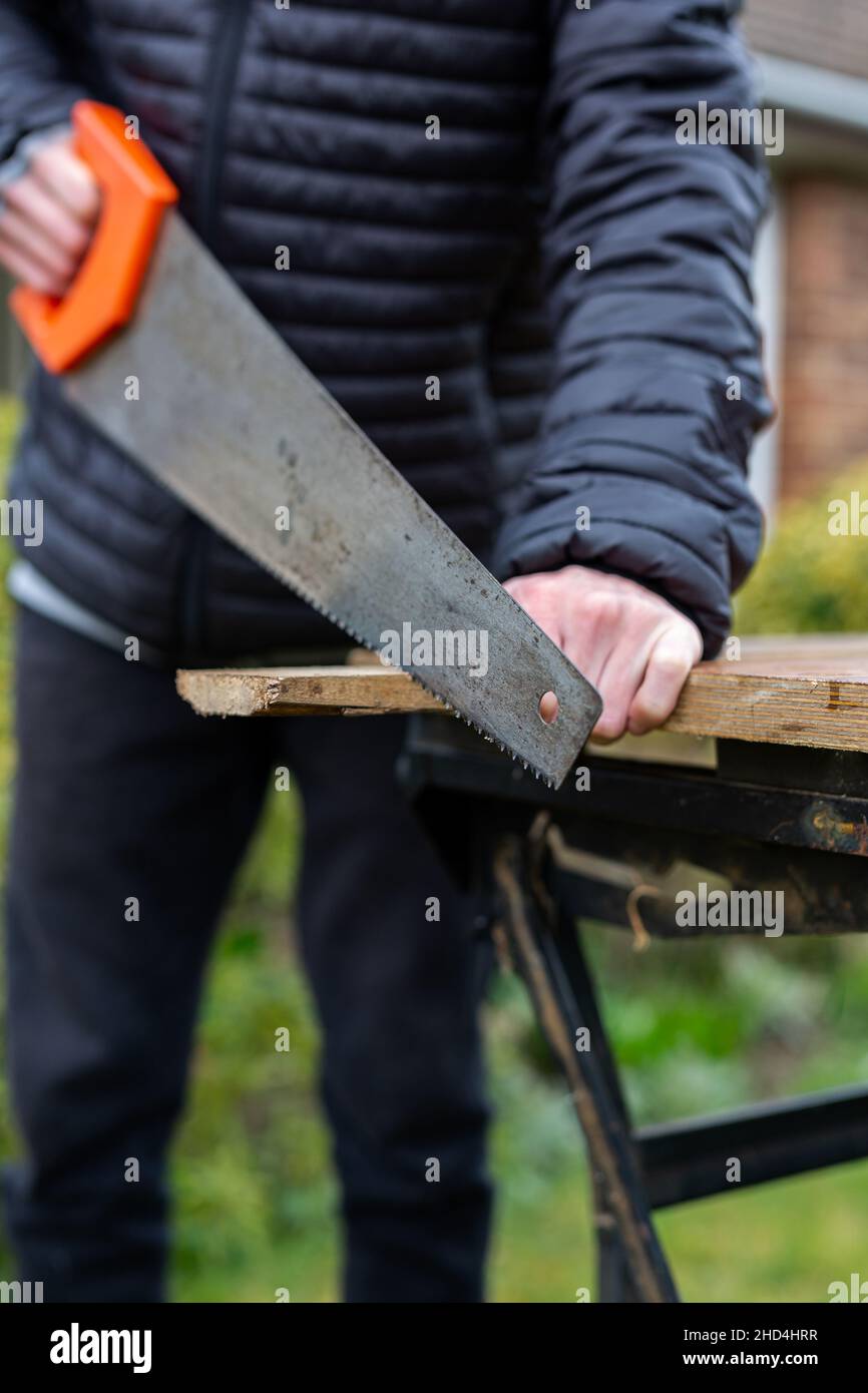 Close up of an unknown person using a hand saw to cut up a plank of ...