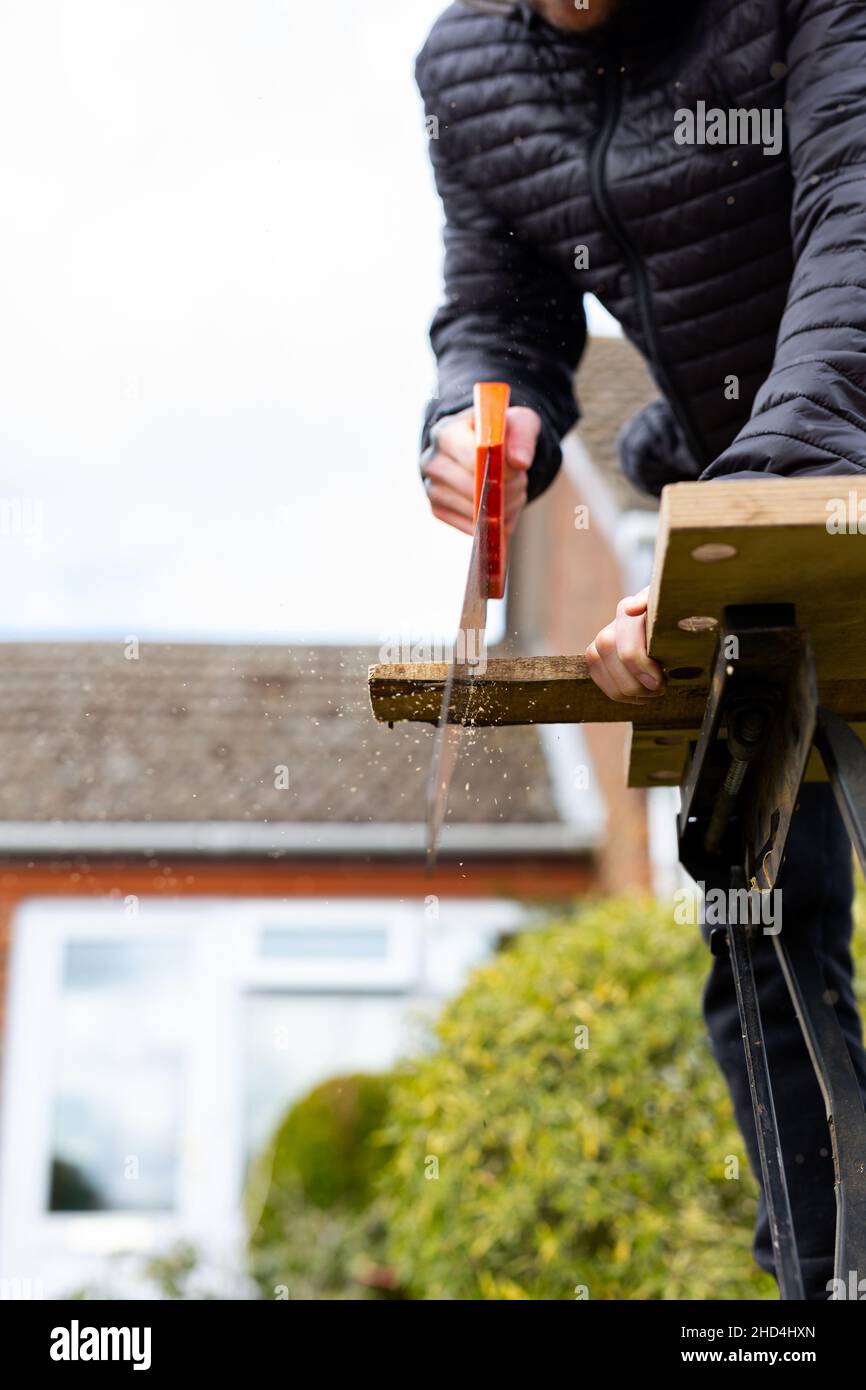 Close up of an unknown person using a hand saw to cut up a plank of ...