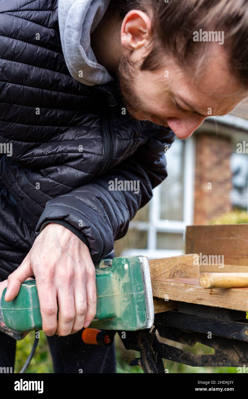 Close up of a young man using a electric belt sander on a DIY project ...